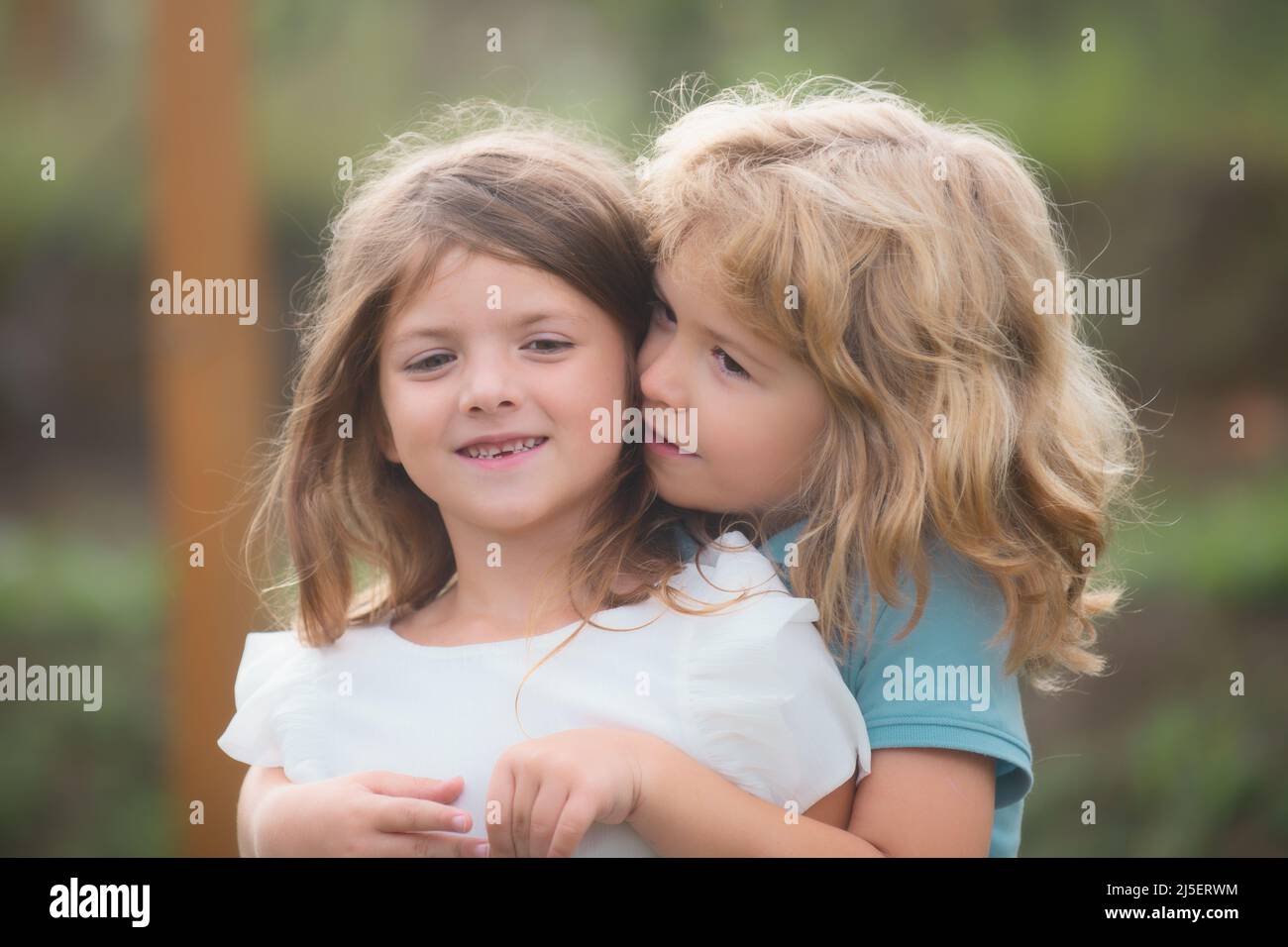 Two little children hug and kiss each other in summer garden. Kids ...