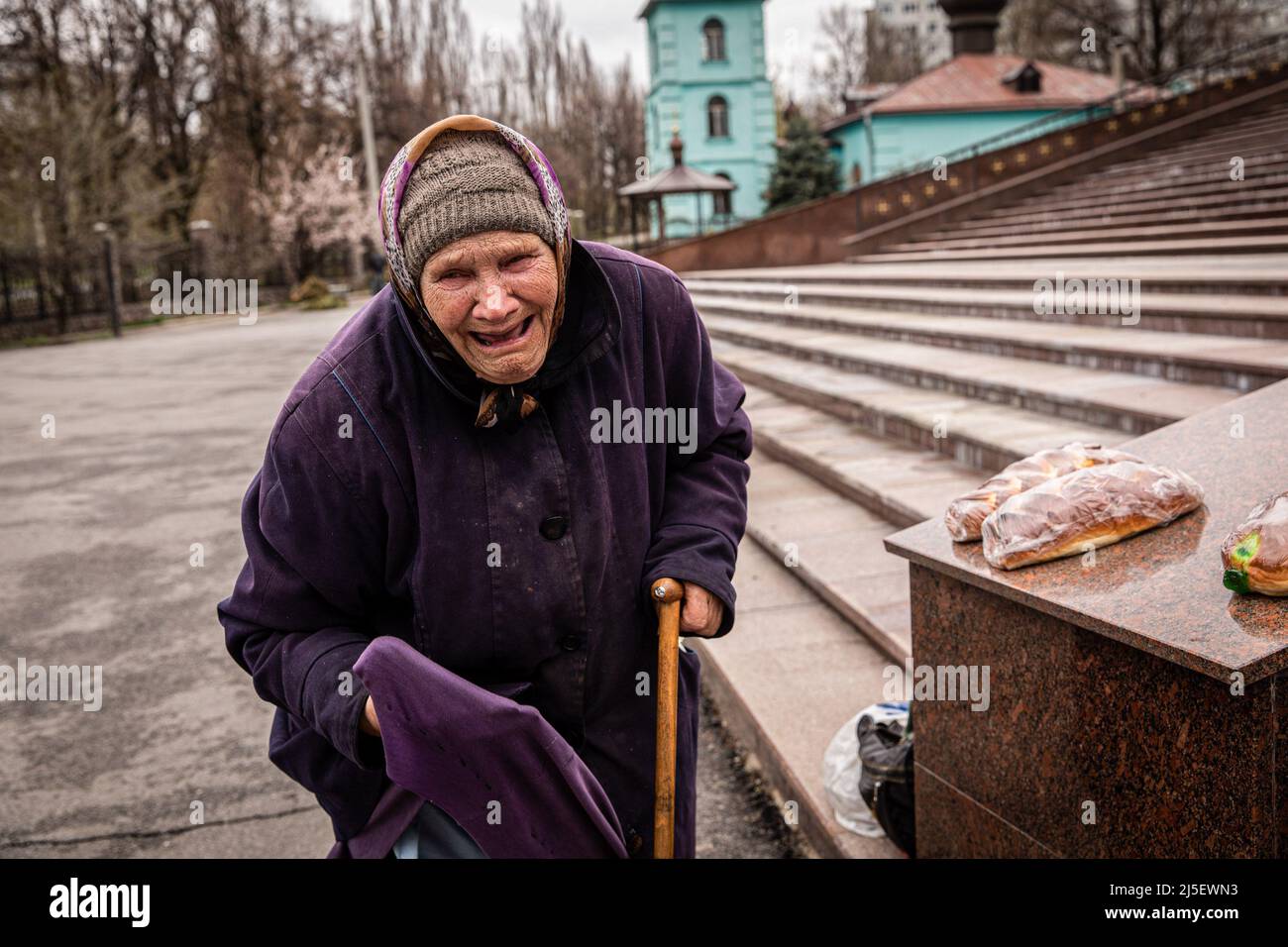 An elderly lady cries in front of the cathedral as she receives bread ...