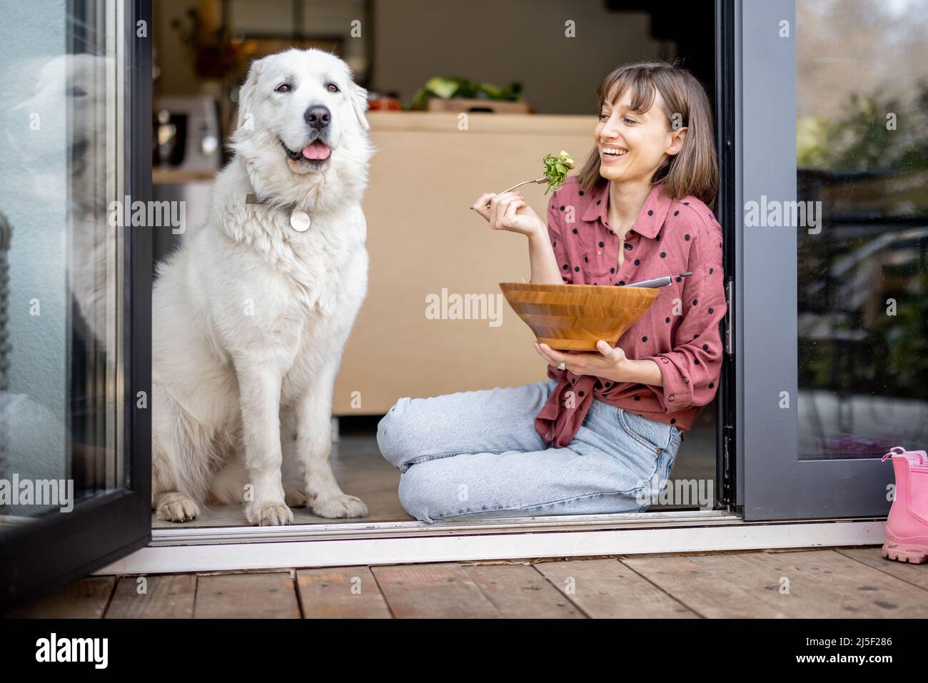 Happy woman eats salad while sitting with her adorable huge white dog ...