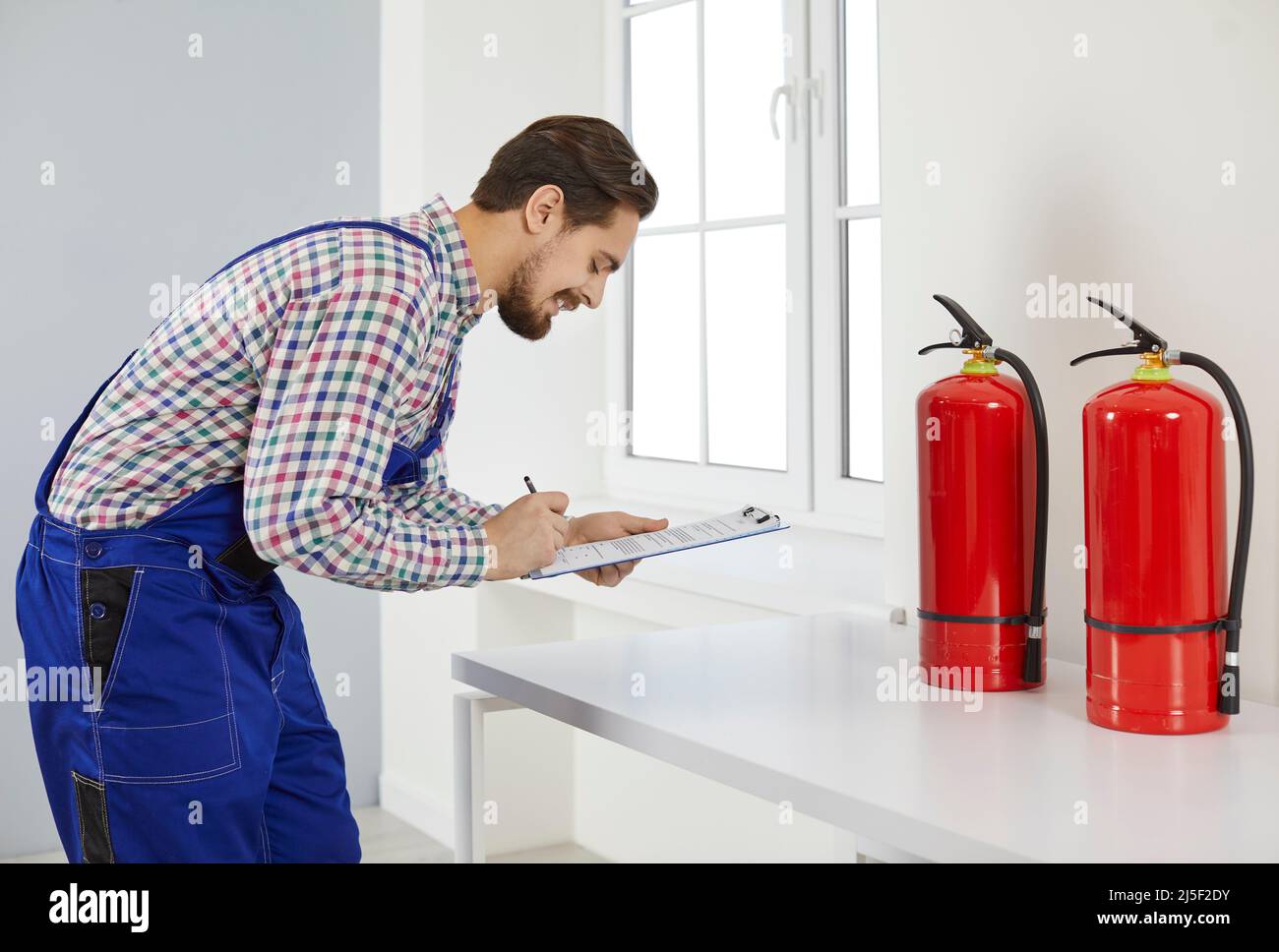 Happy fire safety engineer writing on clipboard while checking ...