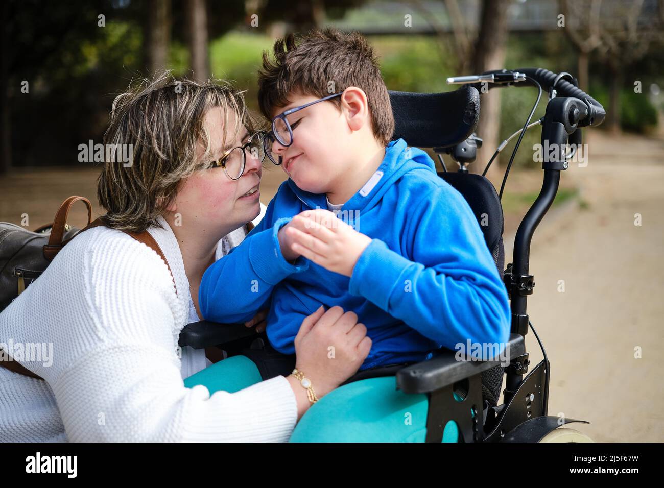 Disabled boy in a wheelchair enjoying the day outdoors with his mother ...