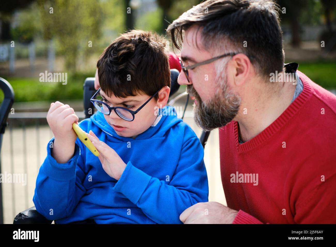 Disabled child on wheelchair using a mobile phone with his father Stock ...