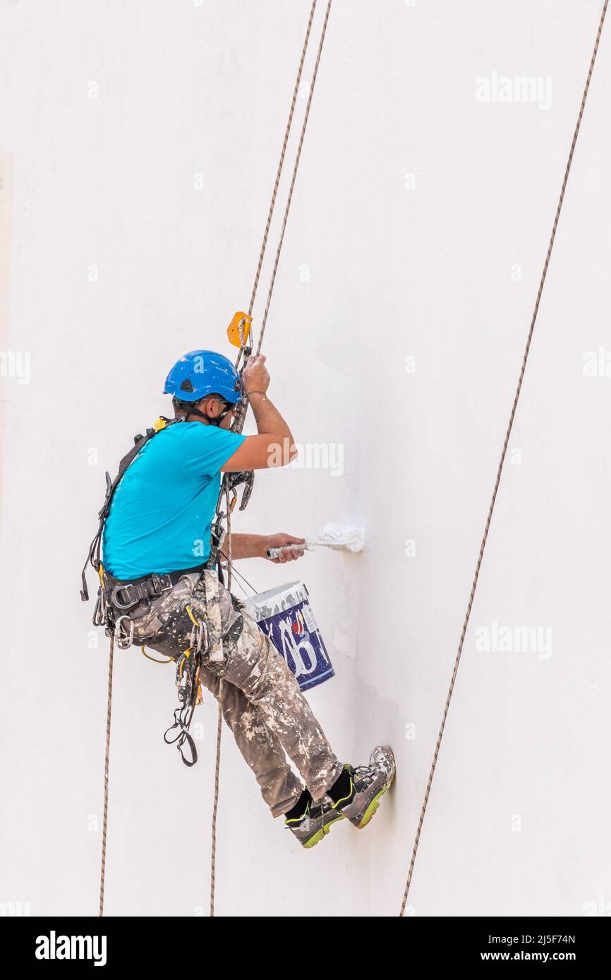 A male worker climbing up the building to paint the facade Stock Photo ...