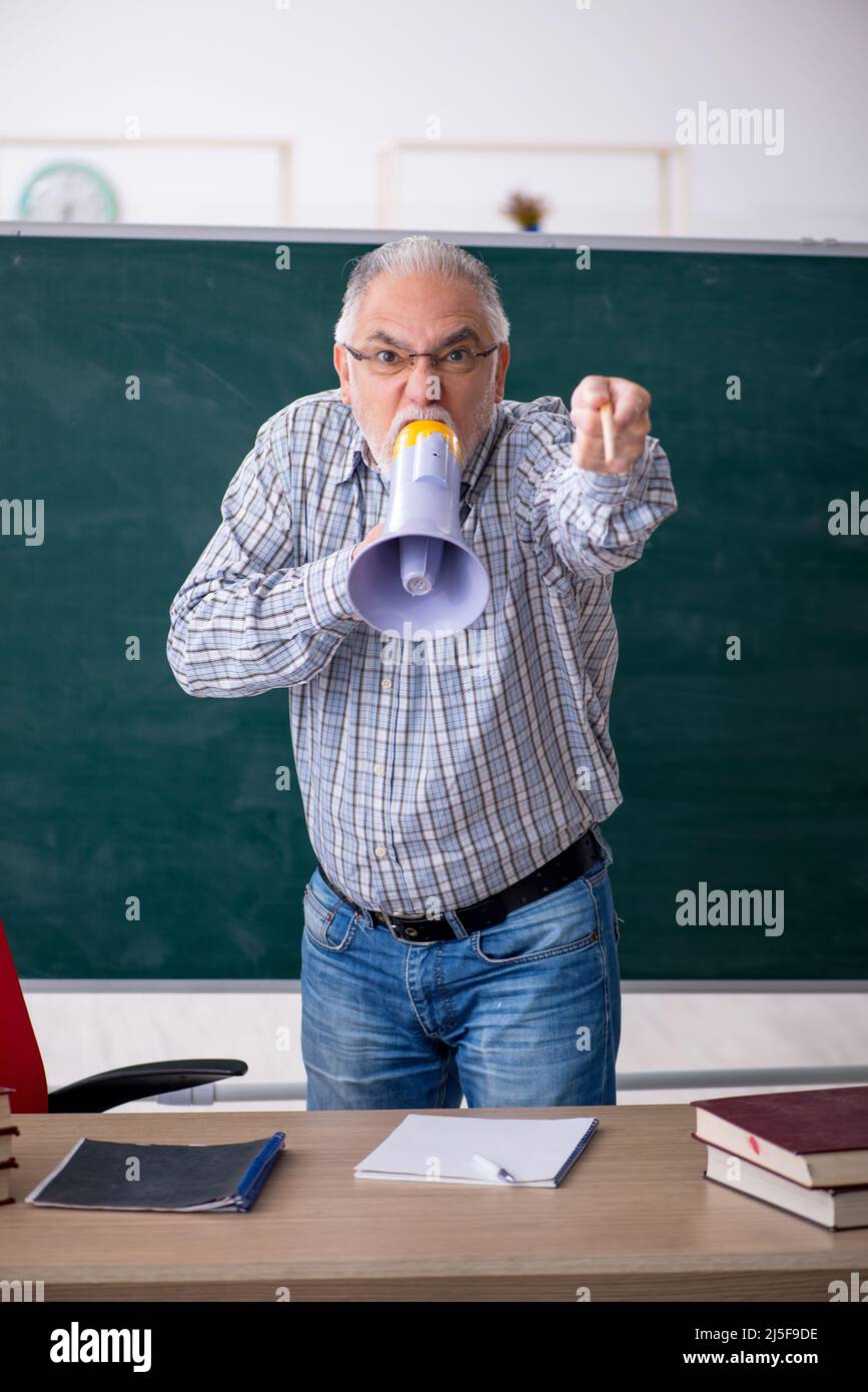 Aged male teacher holding megaphone in the classroom Stock Photo - Alamy
