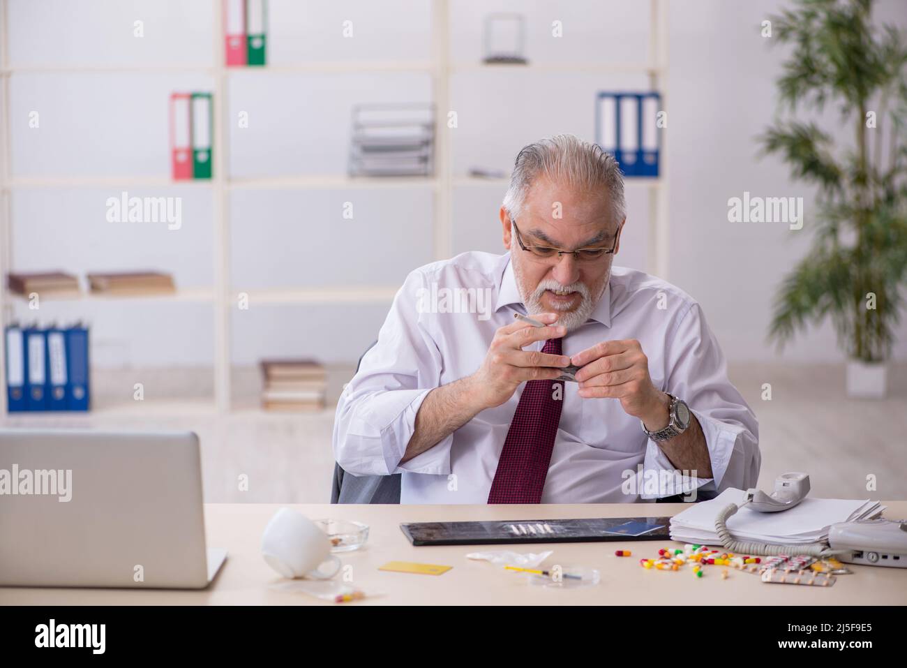 Old male drug addicted employee sitting at workplace Stock Photo - Alamy