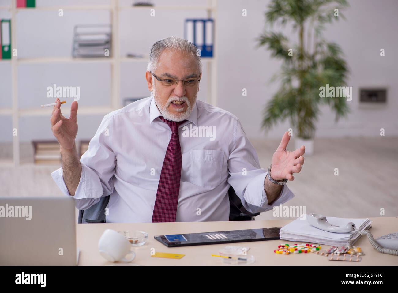 Old male drug addicted employee sitting at workplace Stock Photo - Alamy