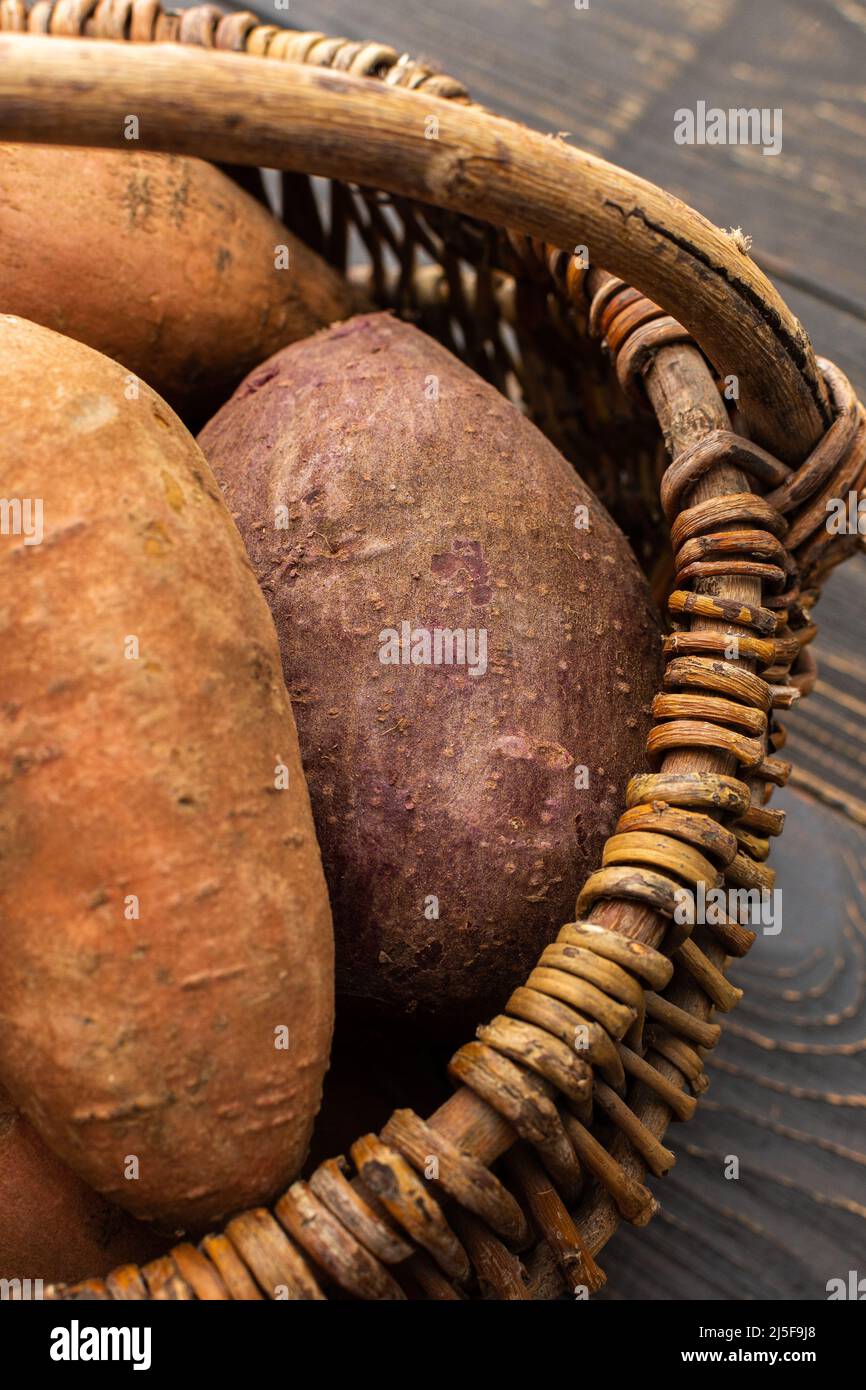 Sweet orange and purple potato tubers in a wicker basket close up on a ...