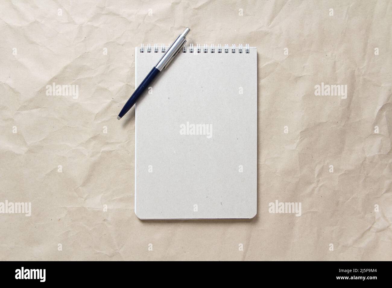 Gray notepad with white coiled spring and pen on a background of beige ...