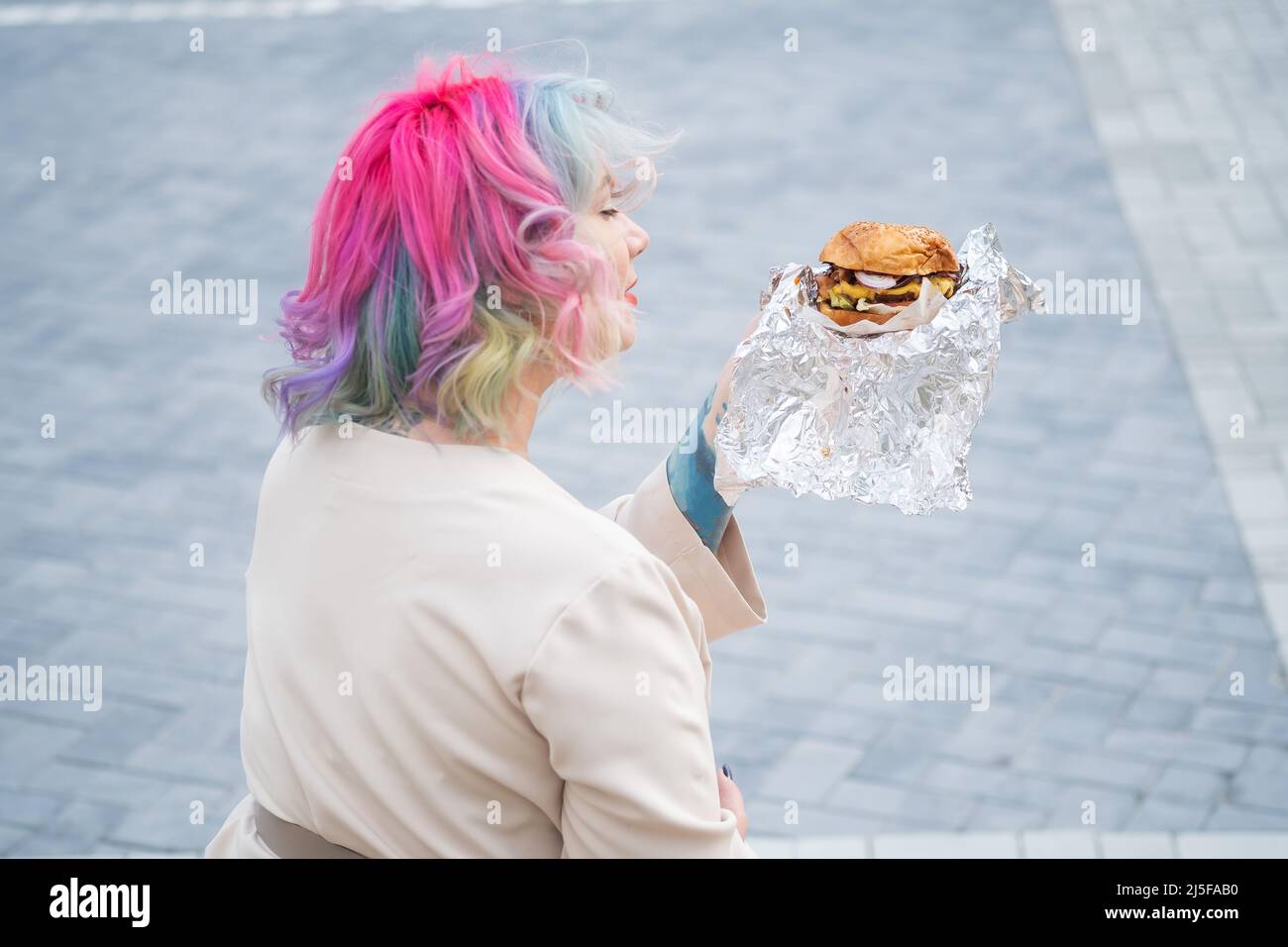 Caucasian woman with curly colored hair eating burger. Bad eating ...