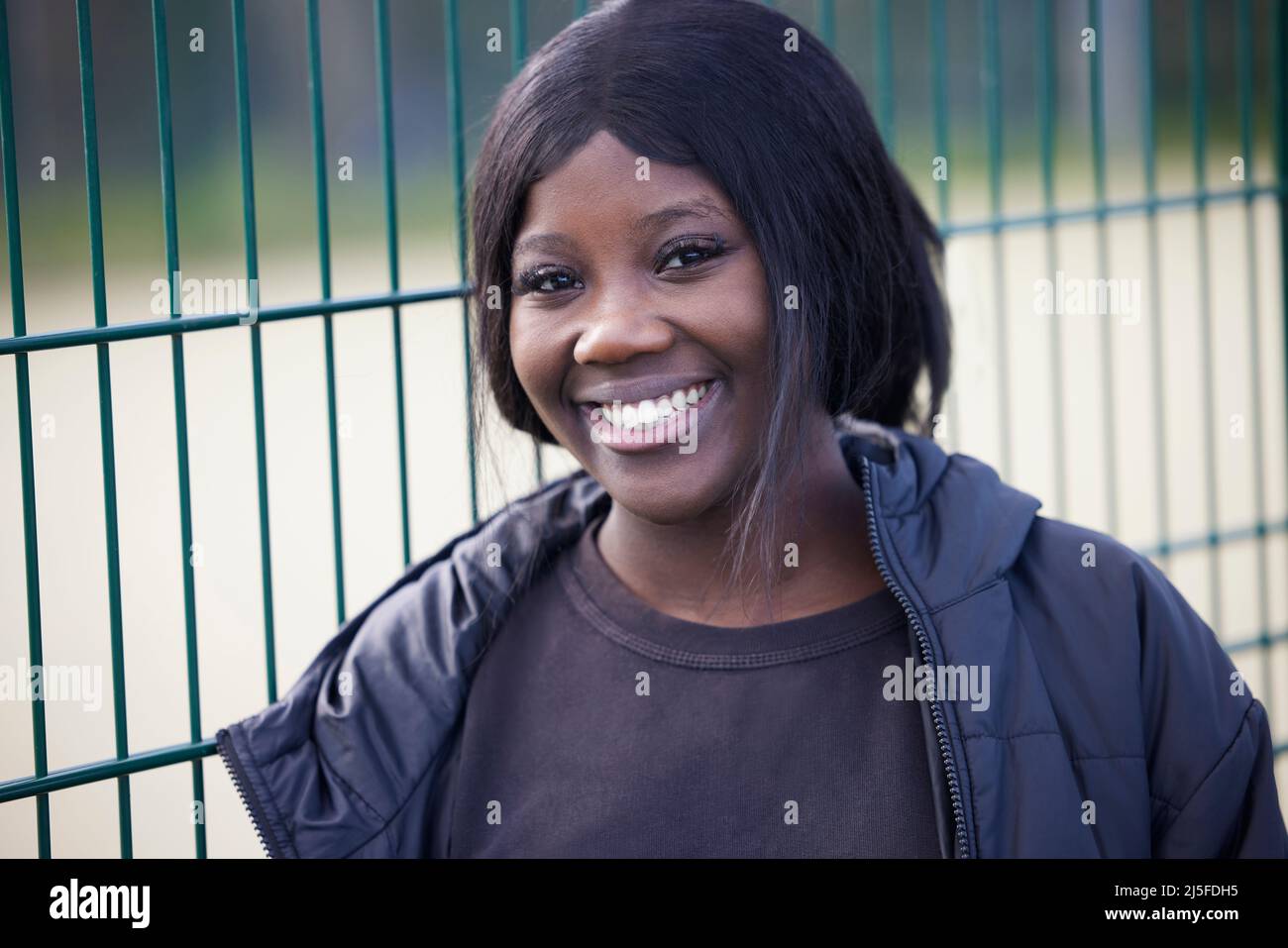Portrait Of Smiling Teenage Girl Leaning Against Fence Outdoors In Park ...