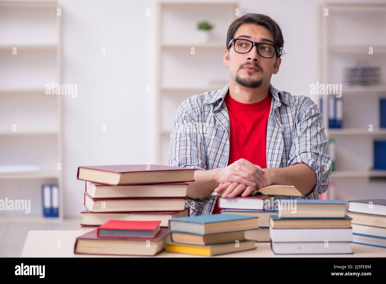 Young student and too many books in the classroom Stock Photo - Alamy