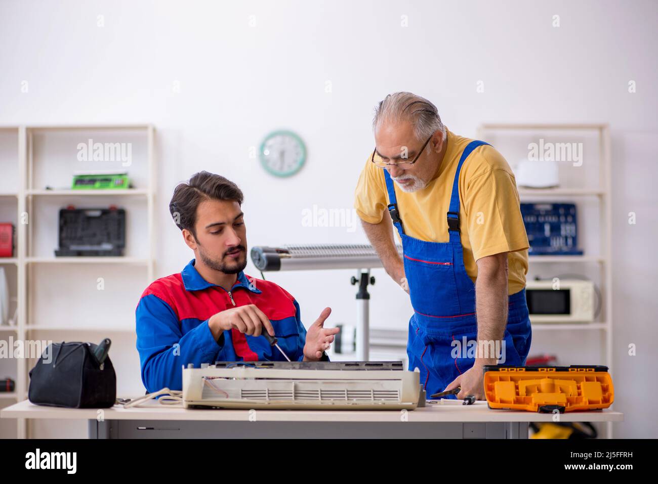 Two repairmen repairing air-conditioner at workshop Stock Photo - Alamy