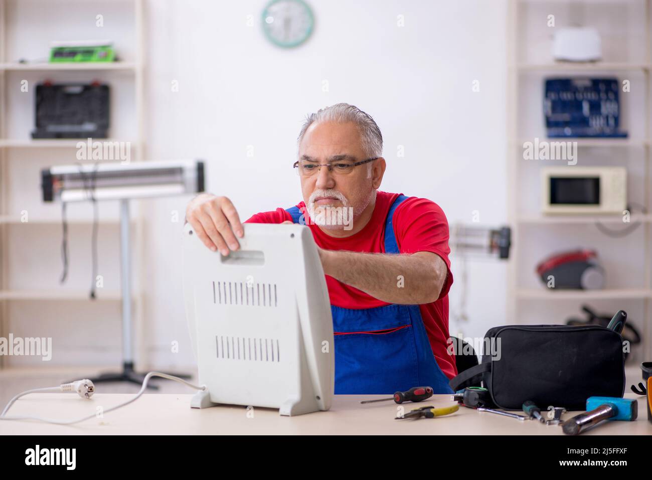 Old male repairman repairing heater at workshop Stock Photo - Alamy