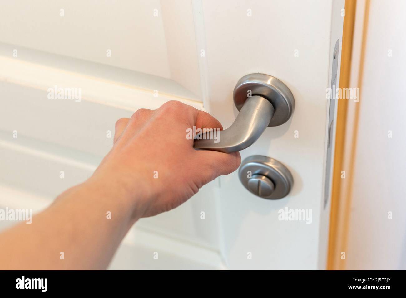Hand presses the doorknob of a white door Stock Photo - Alamy