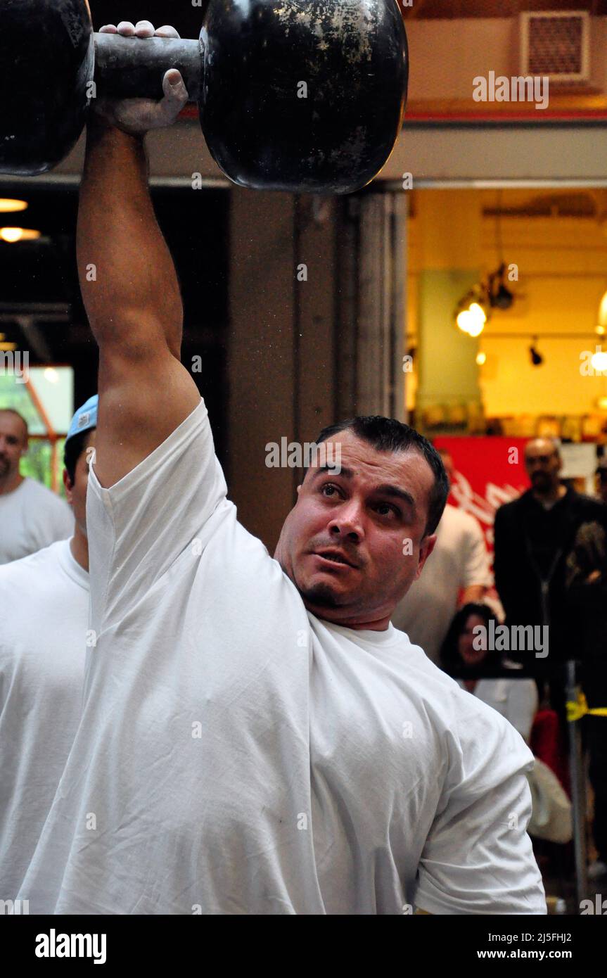 A competitor lifts a dumbell over his head in a Strongman Competition ...