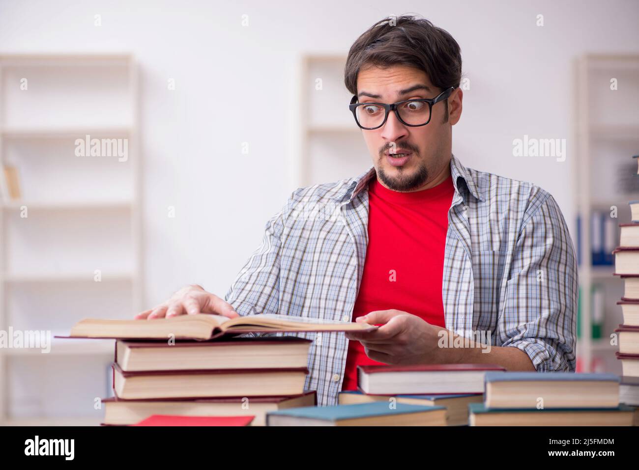 Young student and too many books in the classroom Stock Photo - Alamy