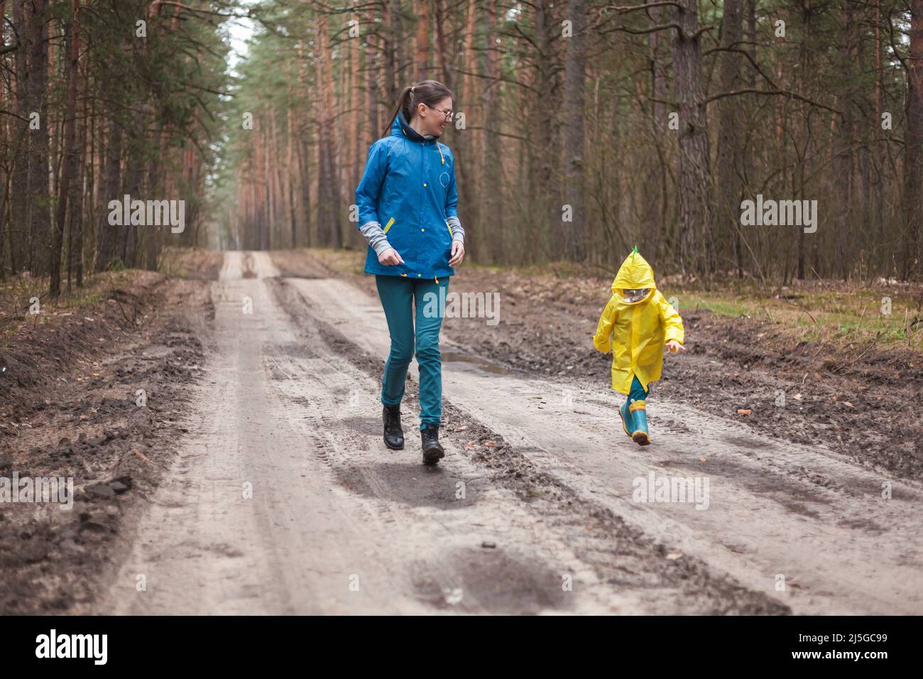Mom and child running along the forest road after rain in raincoats ...