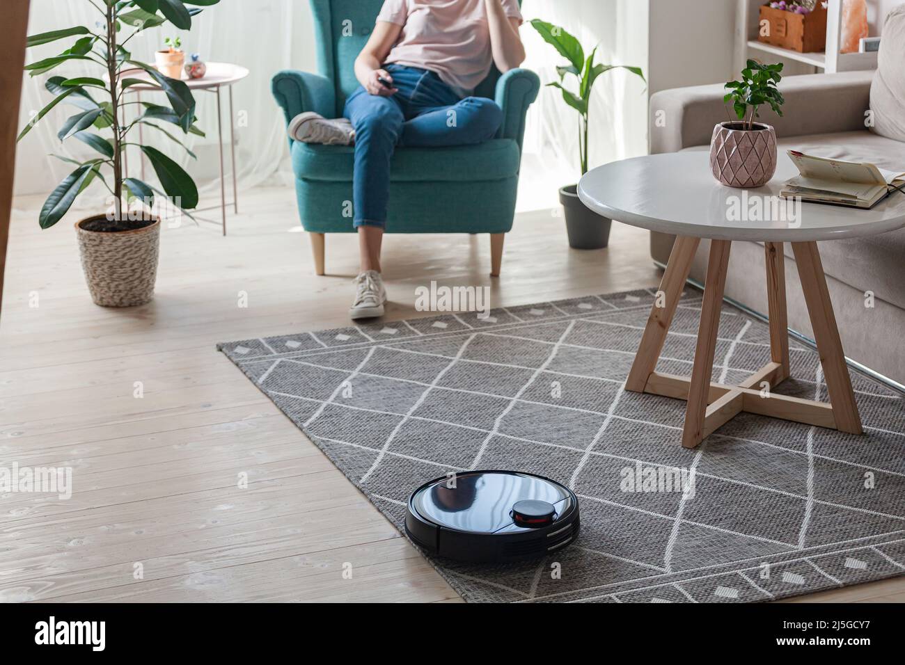 Robotic vacuum cleaner cleaning carpet, woman controls remote control ...