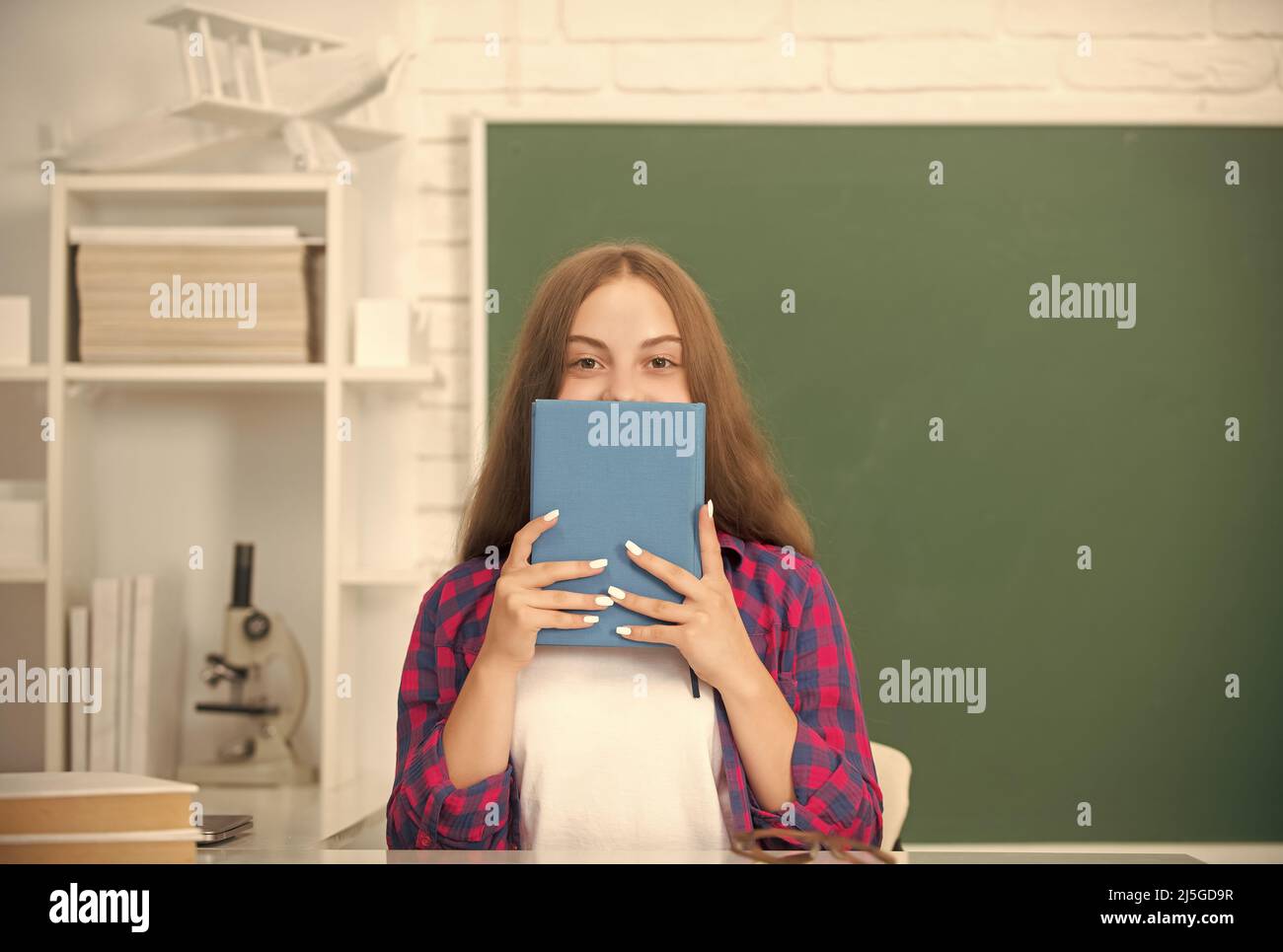 child hiding behind book at school on blackboard background, knowledge ...