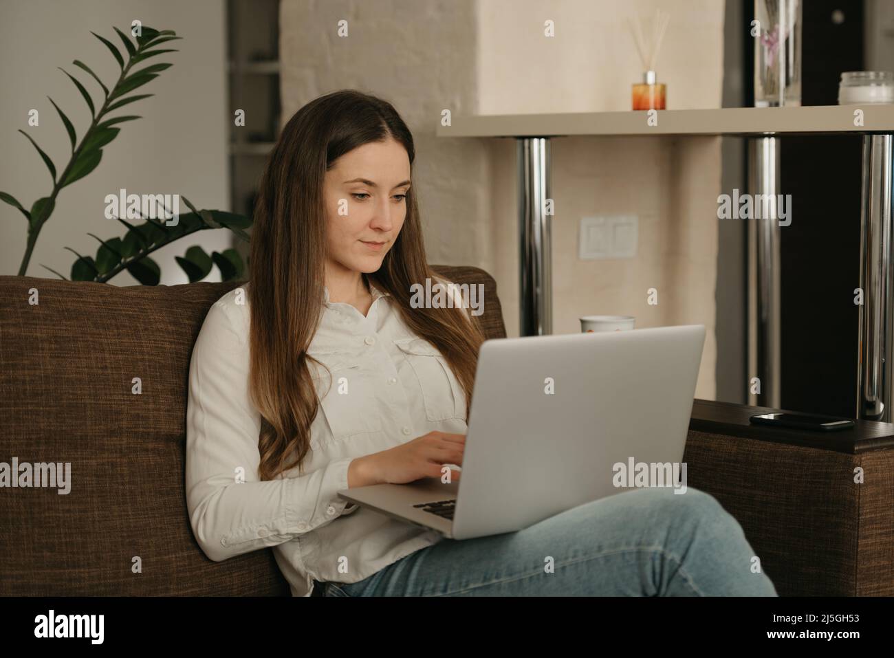 A businesswoman working remotely on her laptop from home on the couch ...
