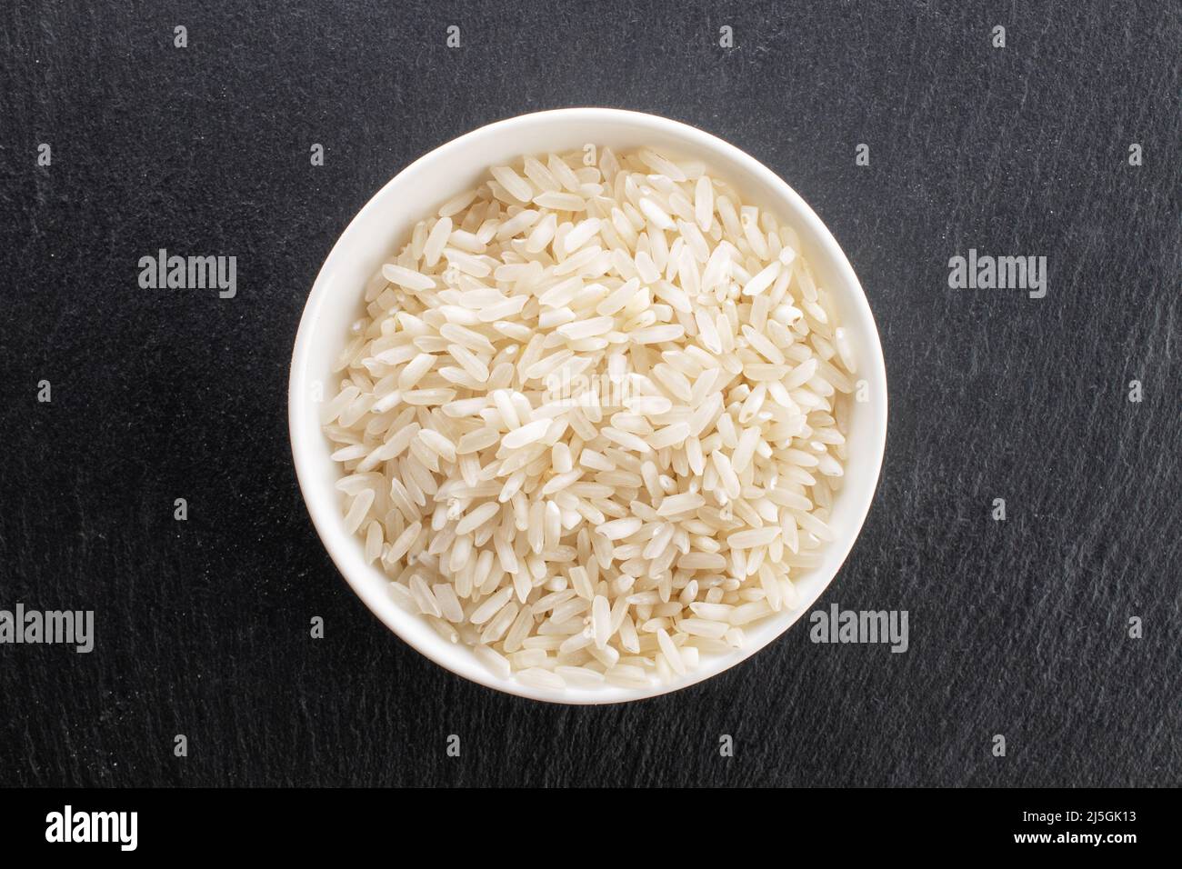 White uncooked rice in a white dish, close-up, on a slate board, top ...