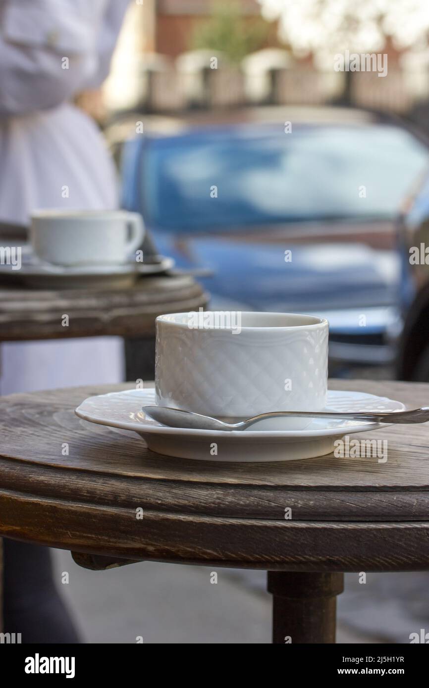 White coffee cup stands on saucer on round wooden table on cafe or ...