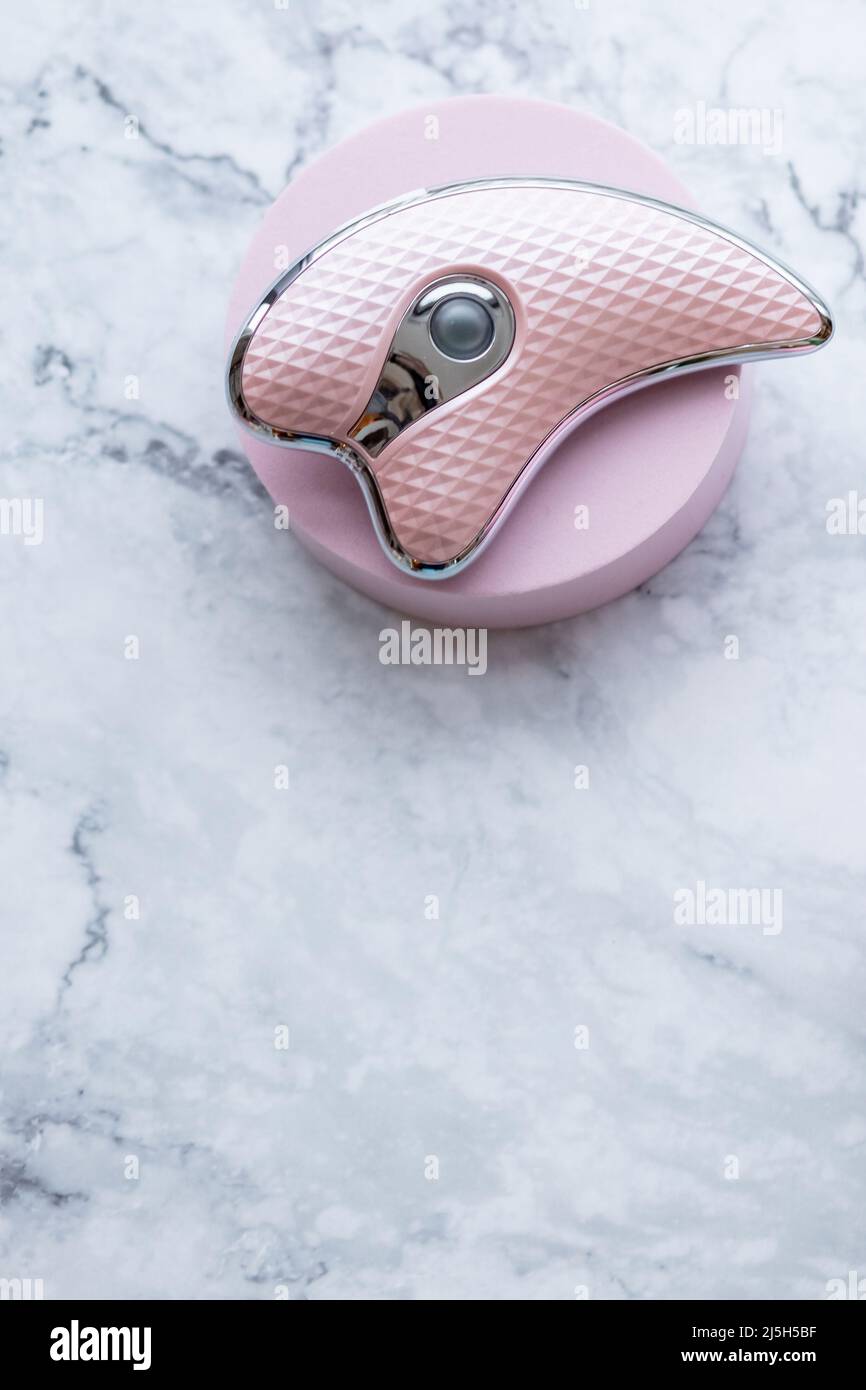 microcurrent facial toning device on pink background with green leaves ...