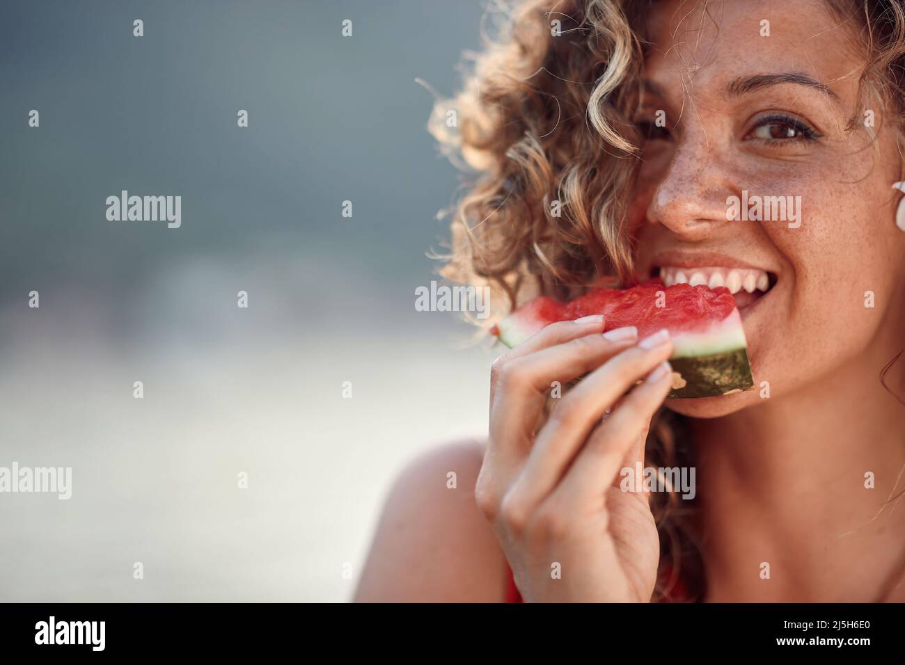 Beautiful young woman with curly hair biting on watermelon piece ...