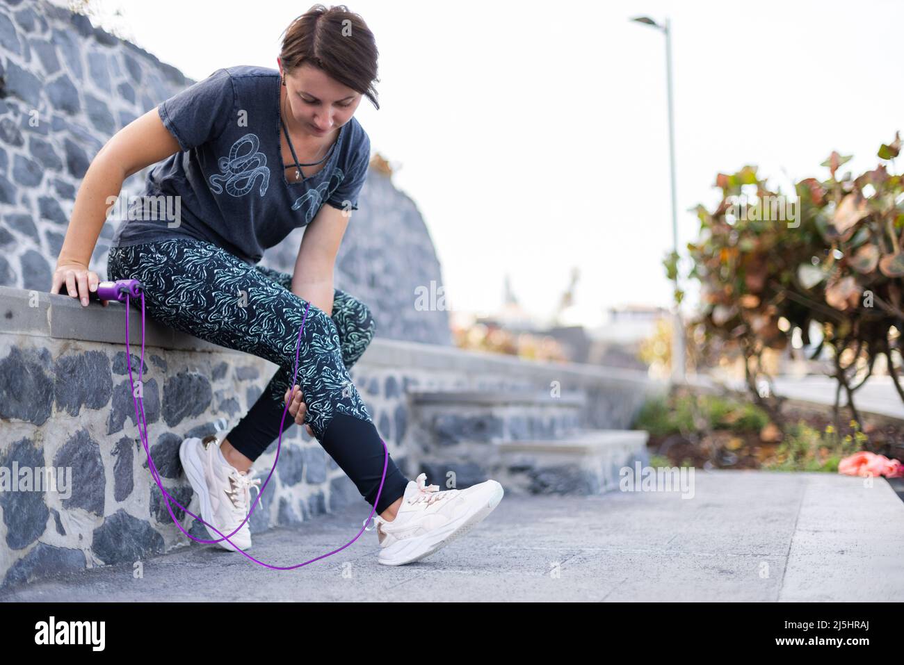 Young woman with a skipping rope. Muscle ache after jumping with a ...