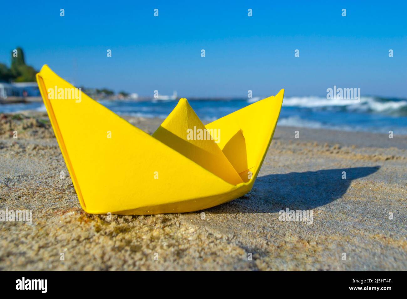 Yellow paper boat on sand on seashore against backdrop of sea waves ...
