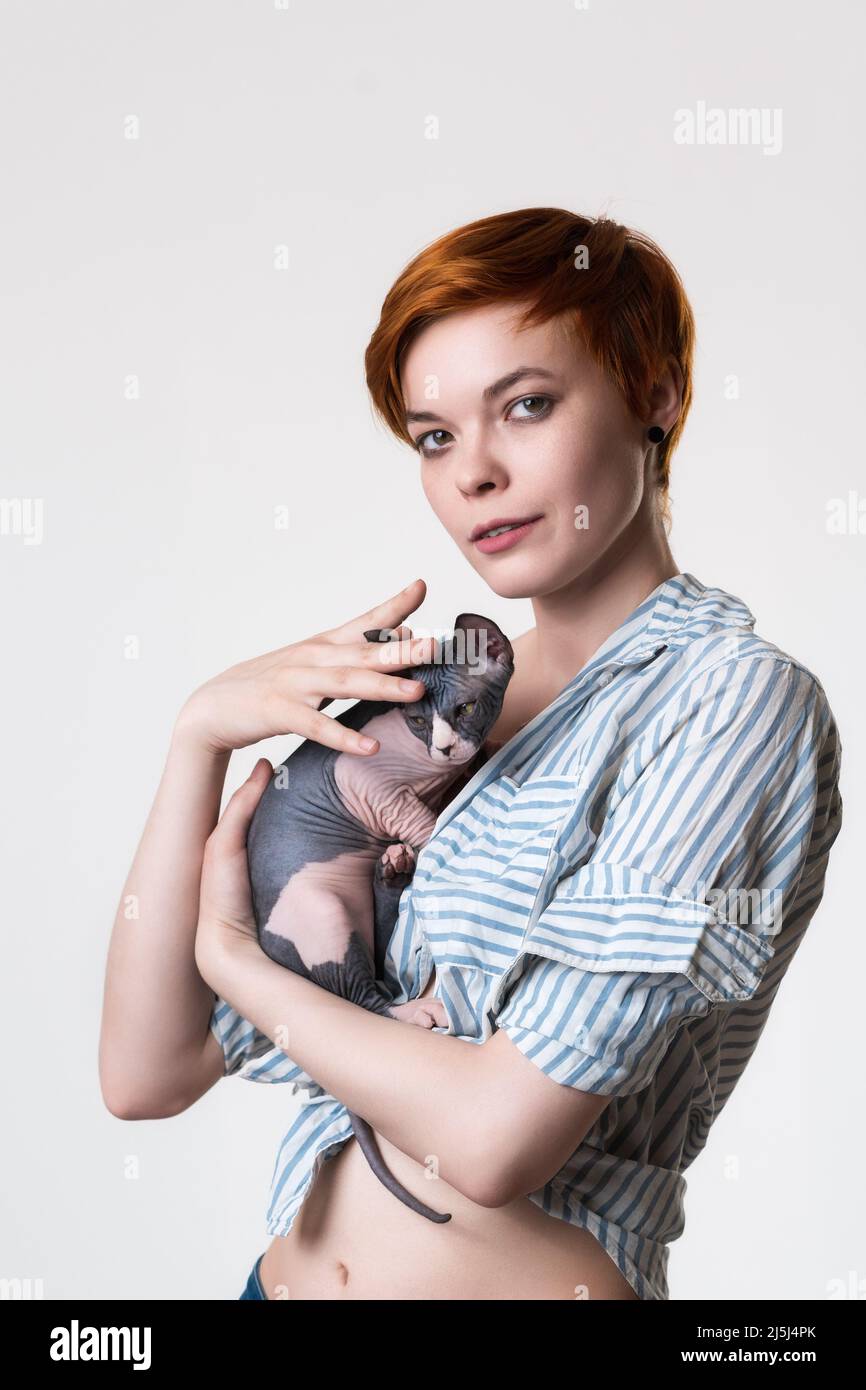 Redhead young woman gently hugging Canadian Sphynx Cat, looking at ...