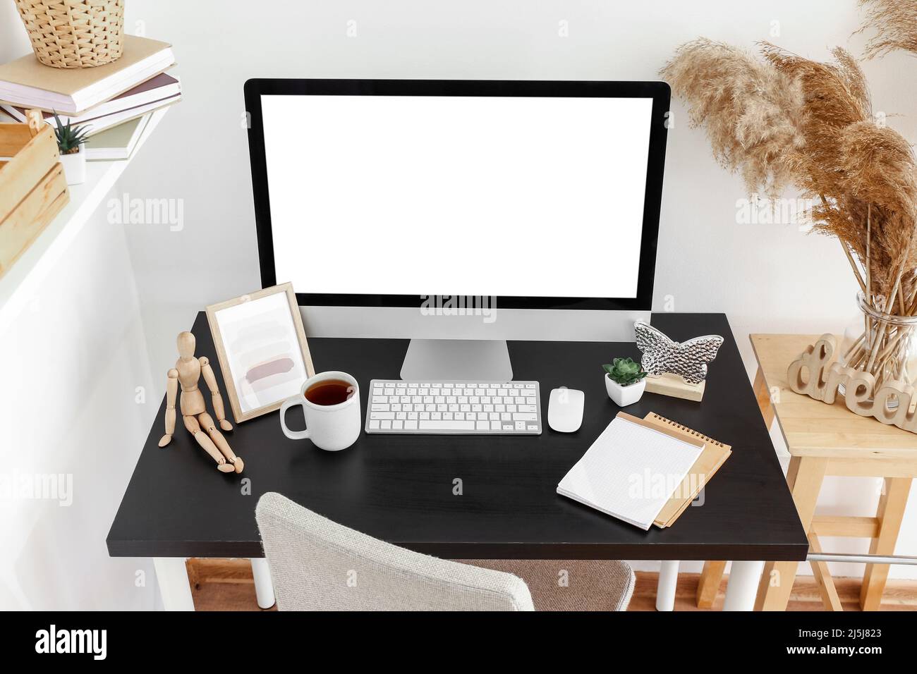 Workplace with computer, cup, notebooks and stylish decor near light ...