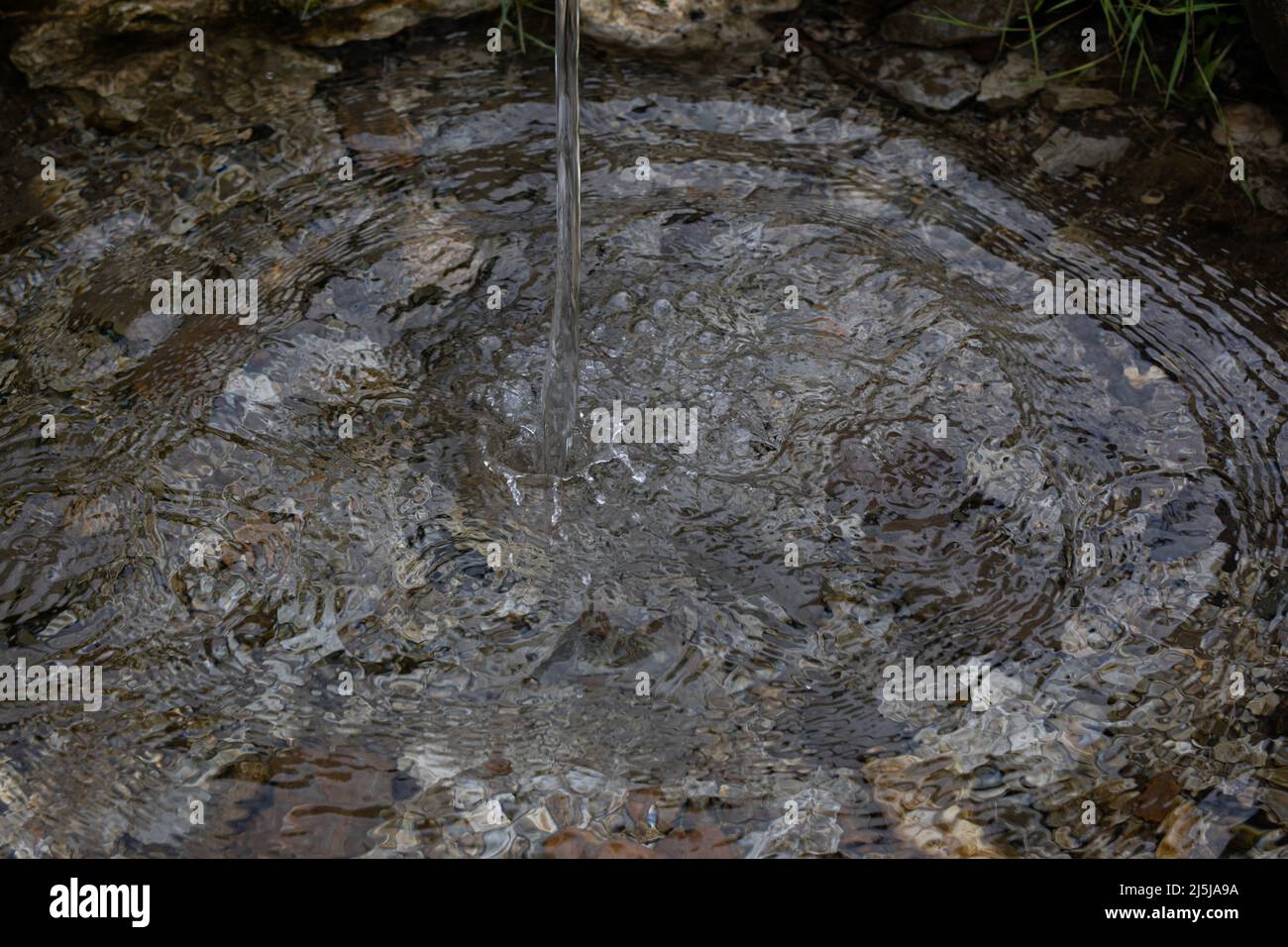 small pure natural stream of water flowing from spring into stone bowl ...