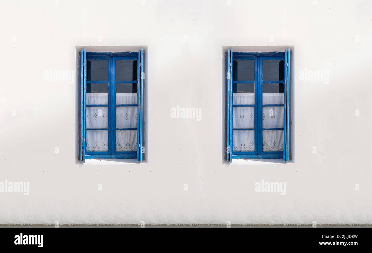Two wooden windows with blue open shutters on white wall background ...