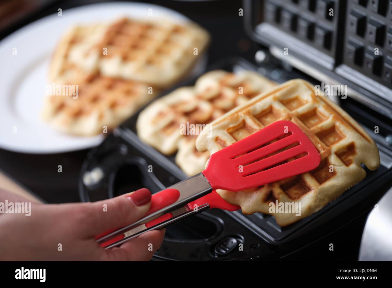 Female hands finishing making waffles on waffle iron in bakery Stock ...