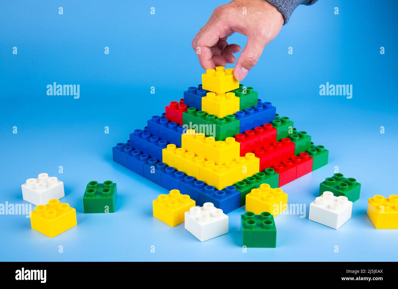 hand building up a wall by stacking up plastic block on blue background ...