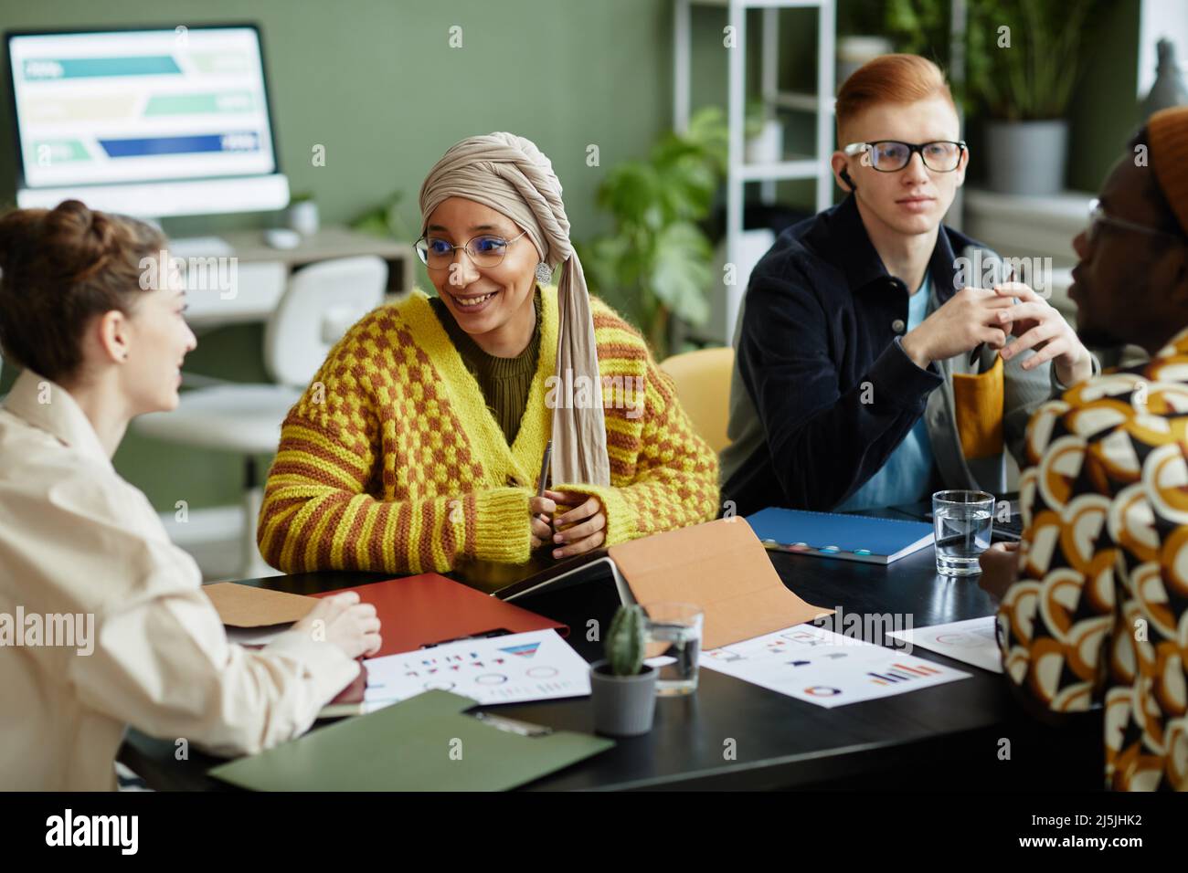 Portrait of creative young woman with team working on project together ...