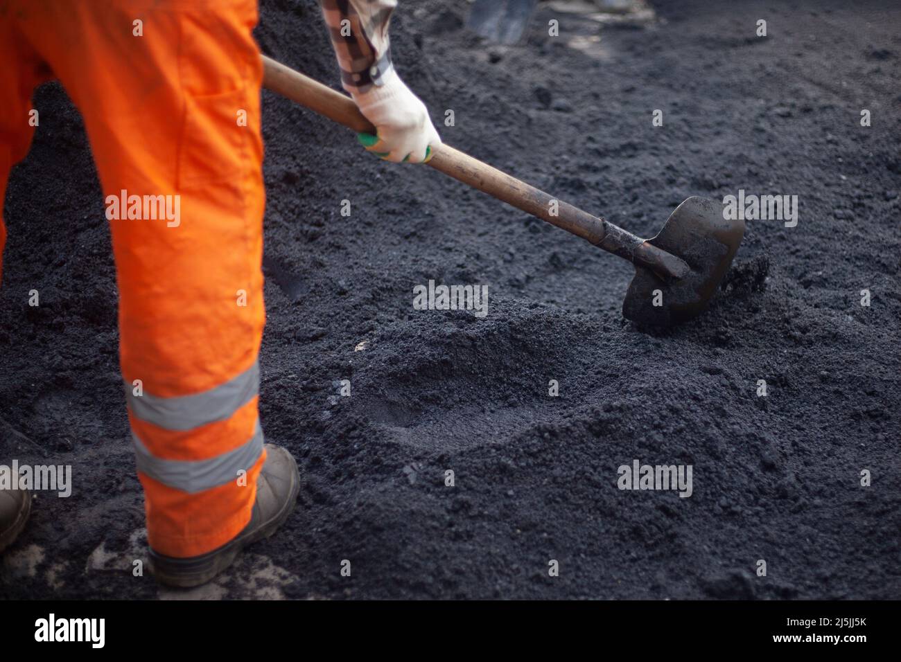 A bunch of asphalt. Workers repair the road. People in orange clothes ...