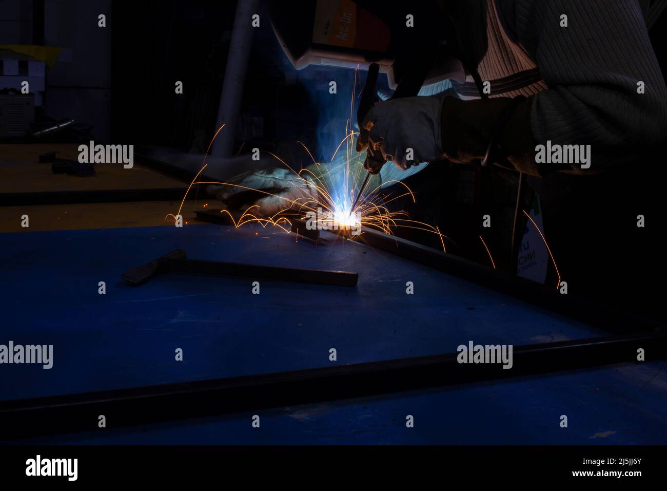 Welding work. A welder in a workshop welds a steel piece. Men's garage ...
