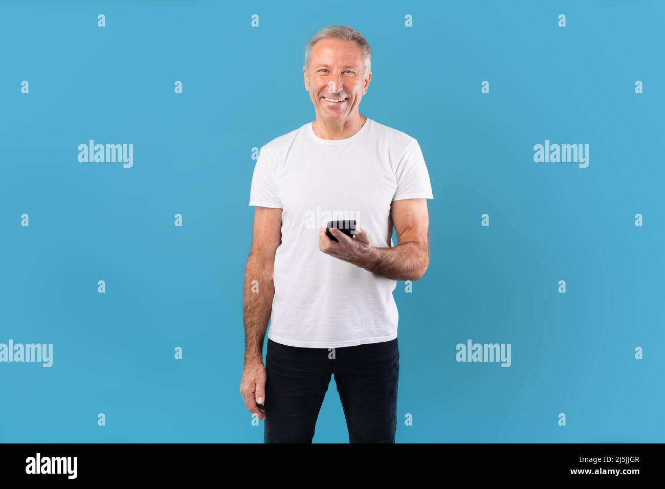 Happy mature man using his mobile phone at blue studio Stock Photo - Alamy