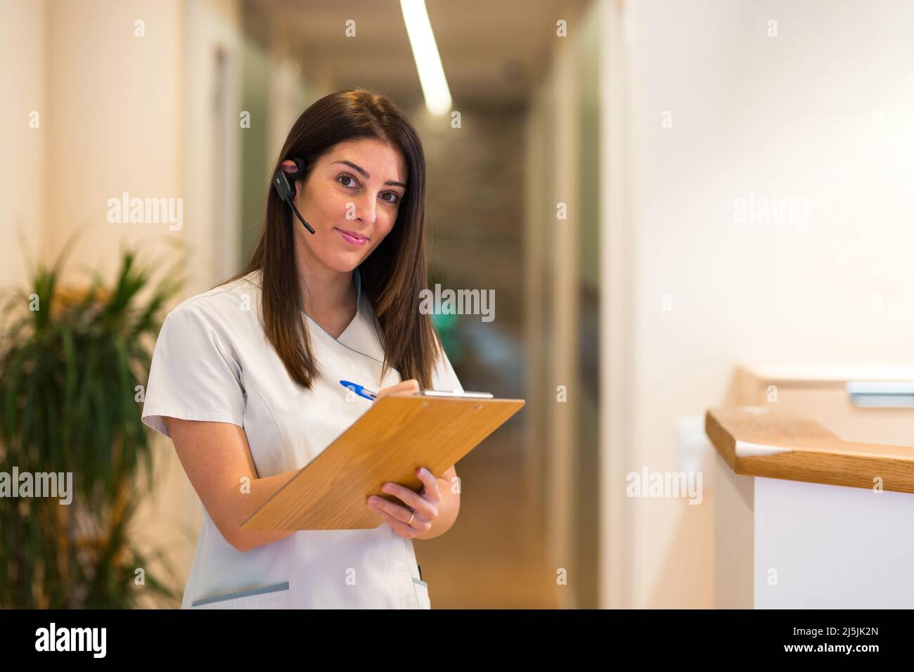 Young woman taking notes on clipboard looking at camera in spa center ...