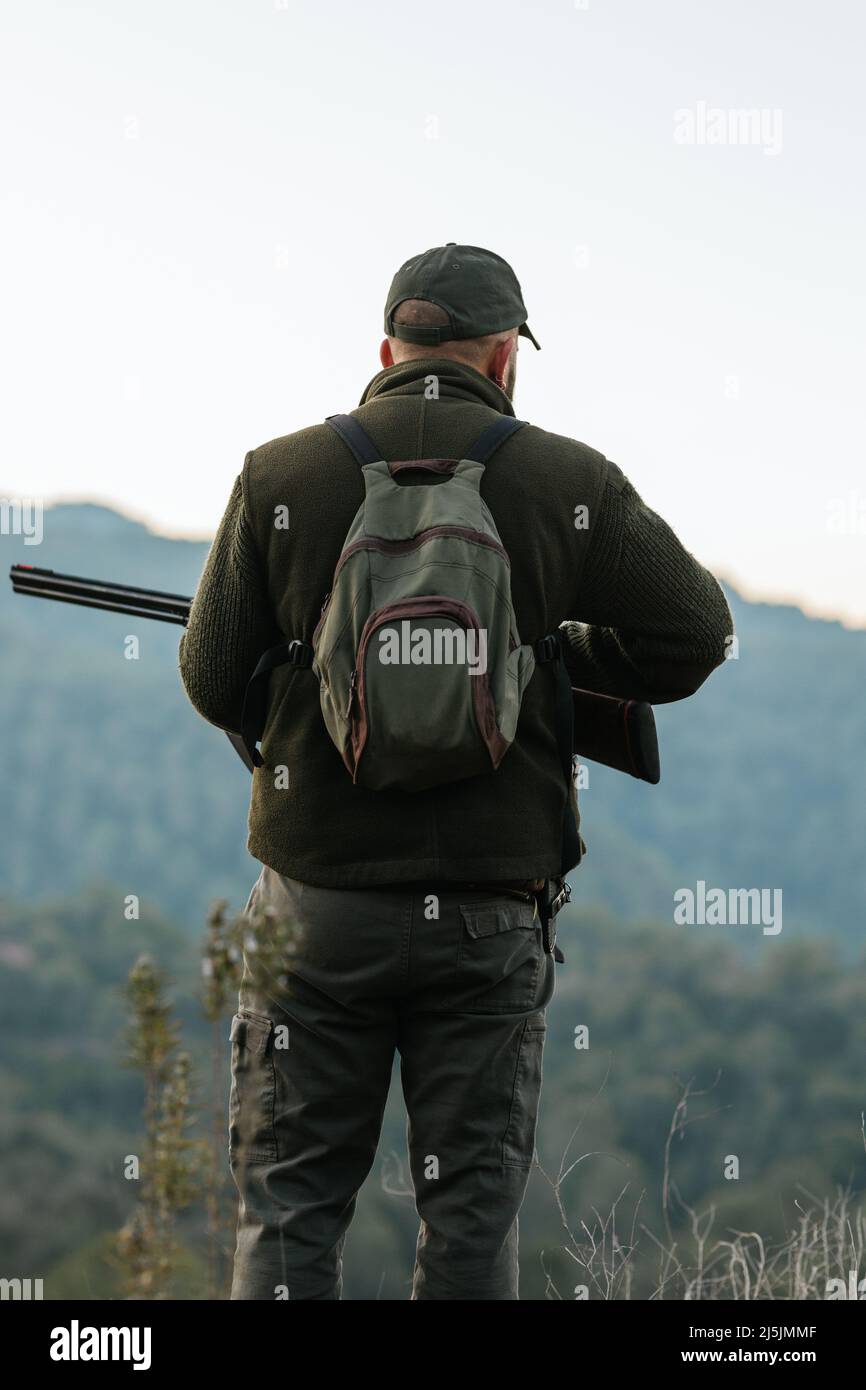 Back view of a hunter holding a shotgun while standing outdoors looking ...