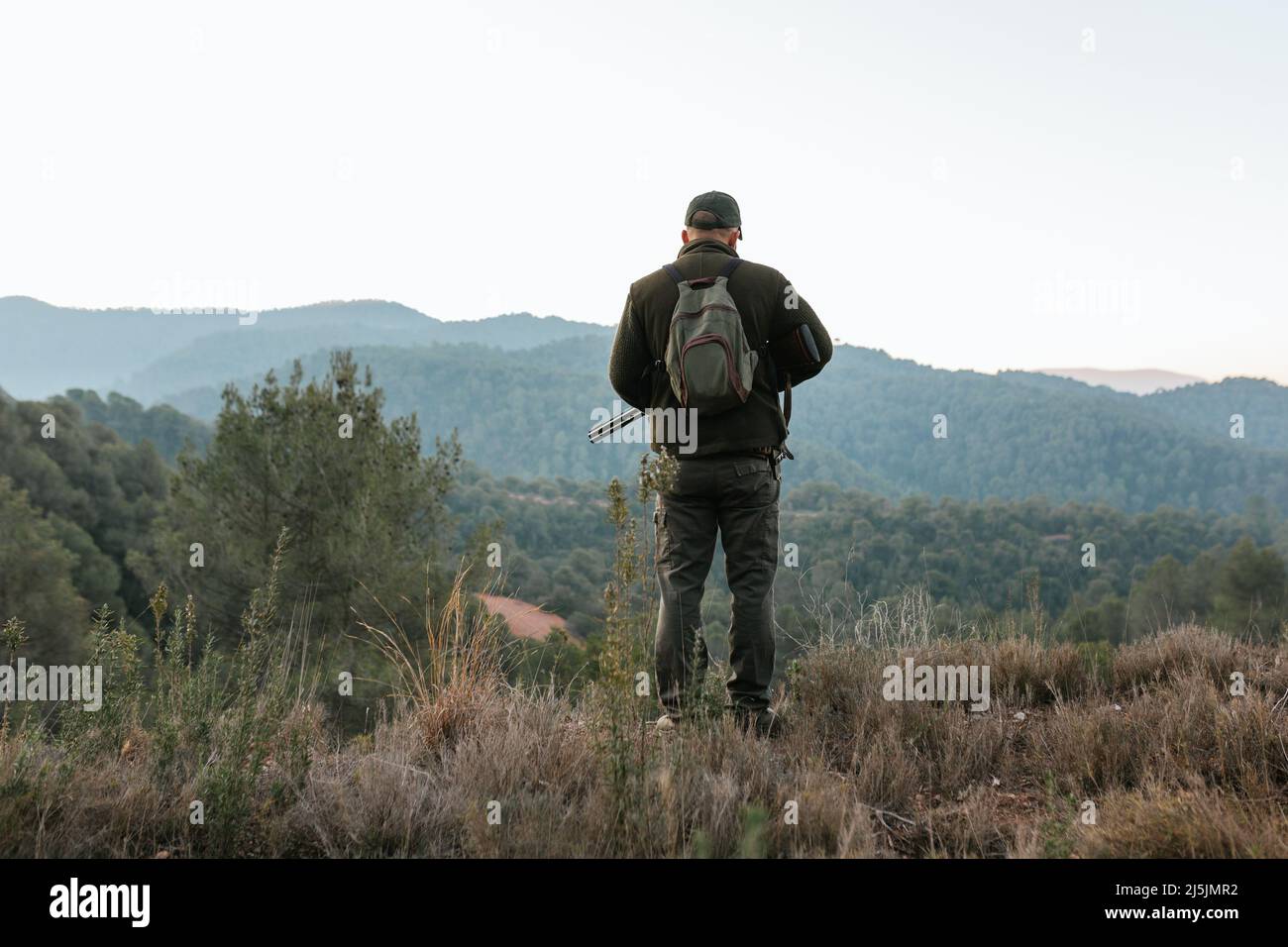 Hunter standing on top of mountain range looking downhill Stock Photo ...