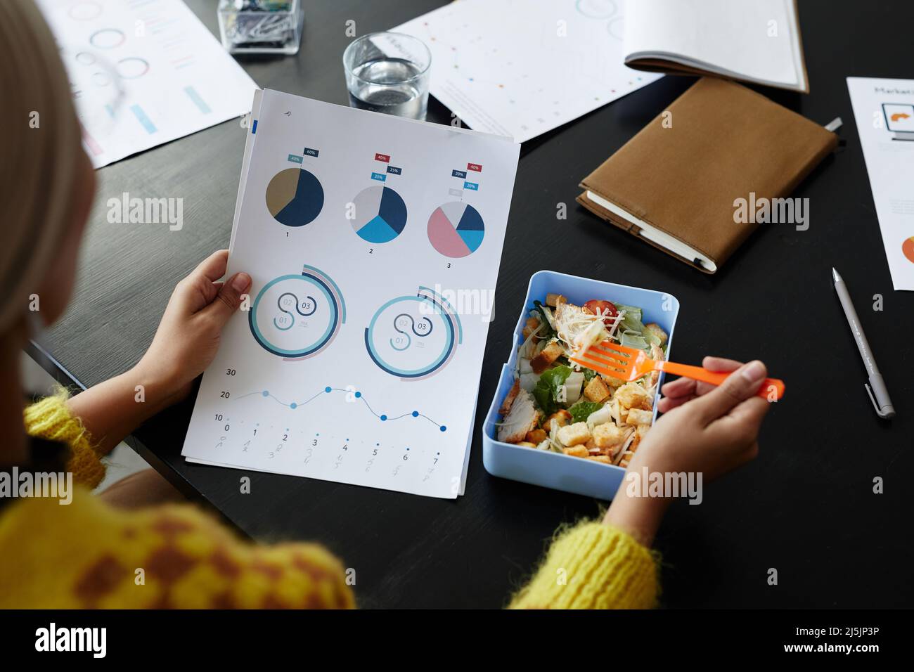 High angle close up of young woman reading data report while eating ...