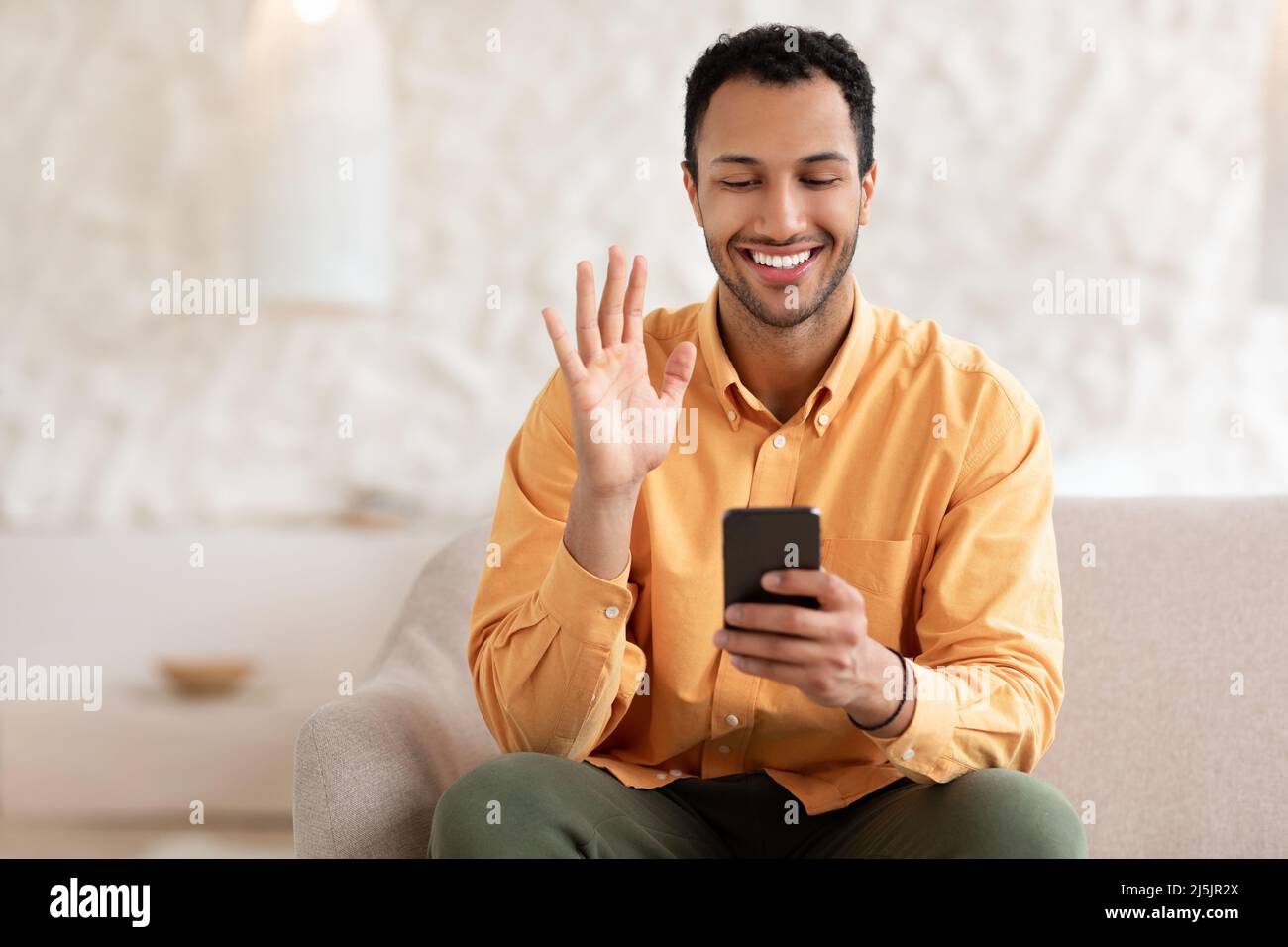 Smiling young man waving hand using mobile phone Stock Photo - Alamy