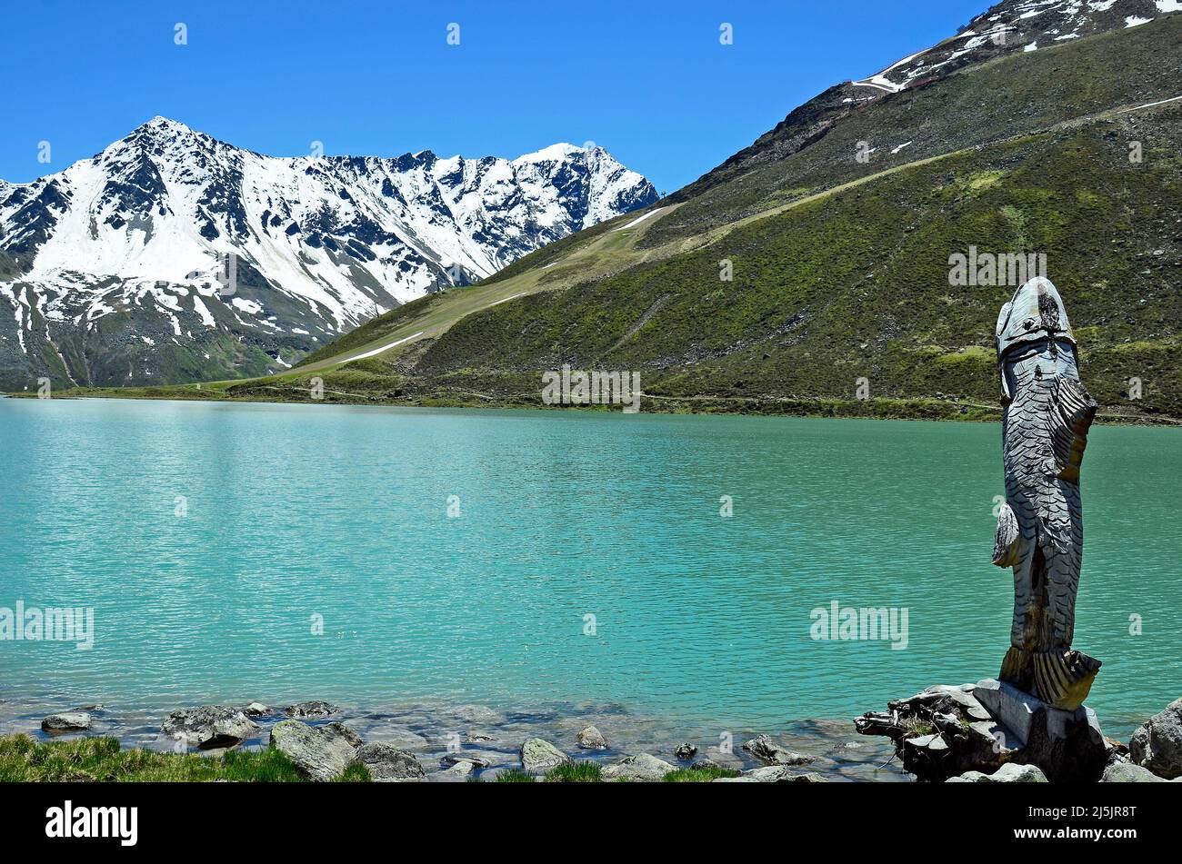 Austria, Tirol, Rifflsee lake with wooden fish sculpture and snow ...