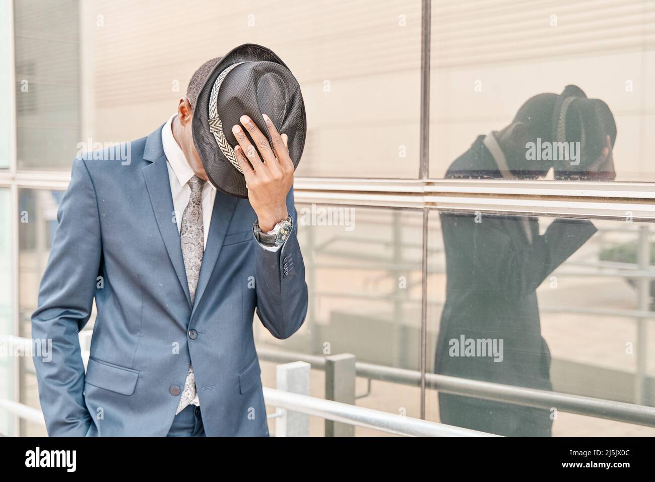 Man in suit hiding face behind his hat. businessman is reflected in ...