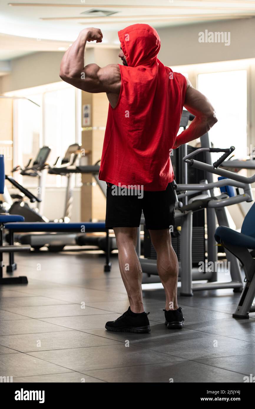Young Man Standing Strong In The Gym And Flexing Muscles in a Red ...