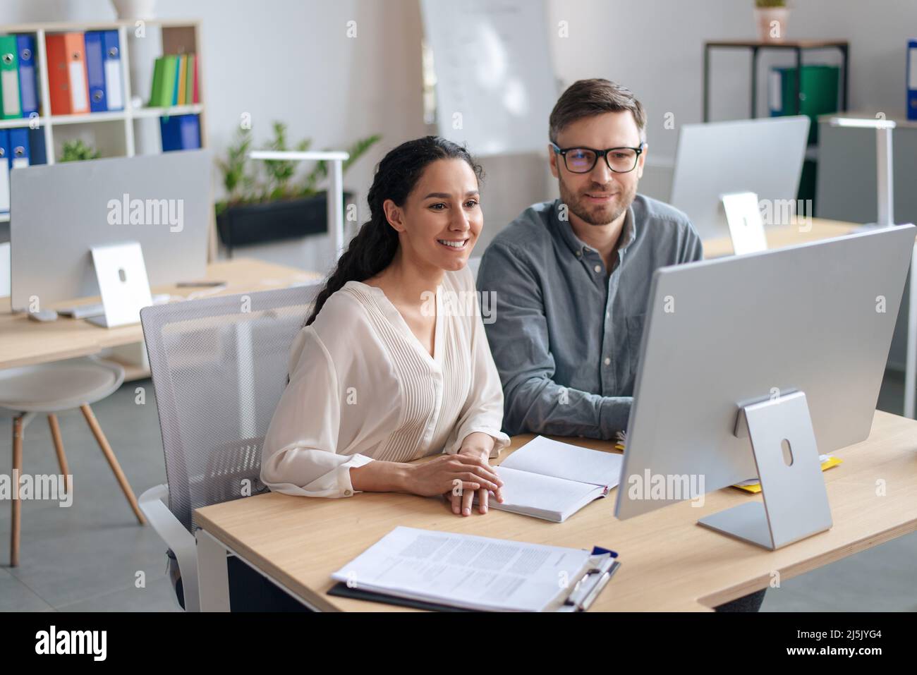 Happy young woman and her male colleague working together, using modern ...