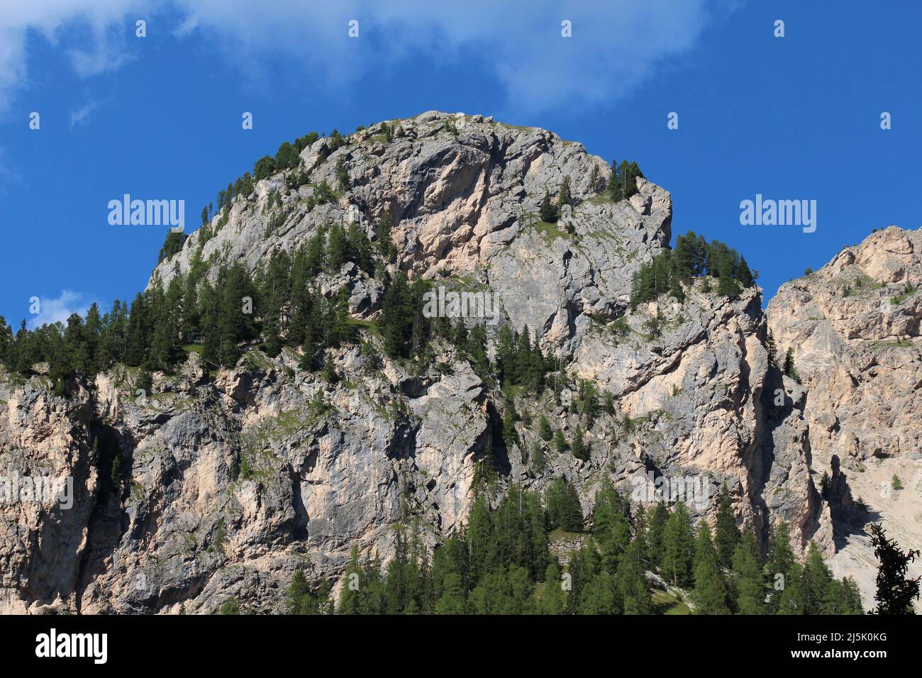 The view of a mountain massif through green forest in a sunny day. Val ...